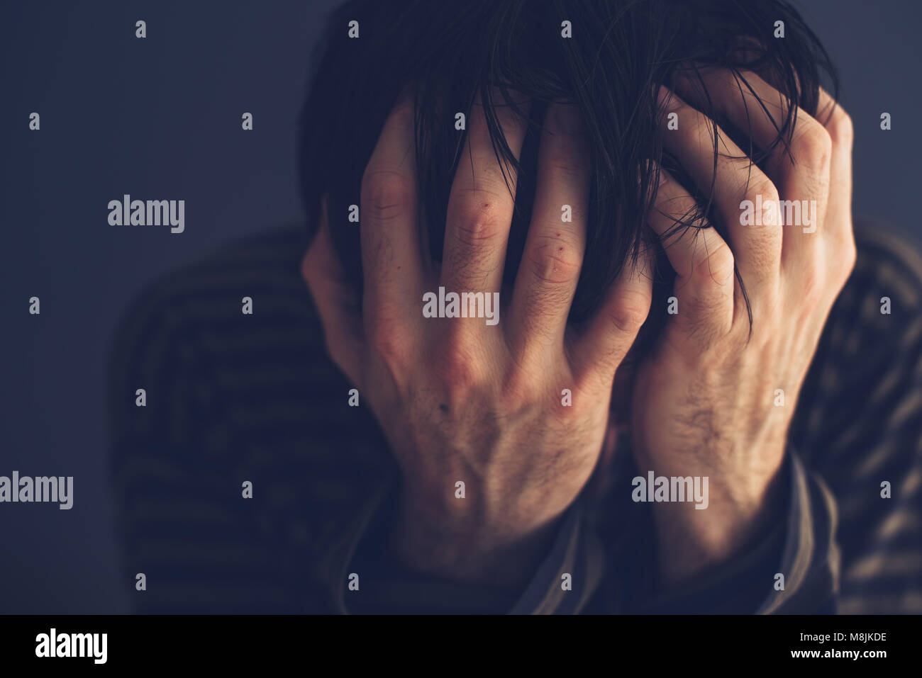 Hopeless drug addict holding his head, low key portrait with selective ...