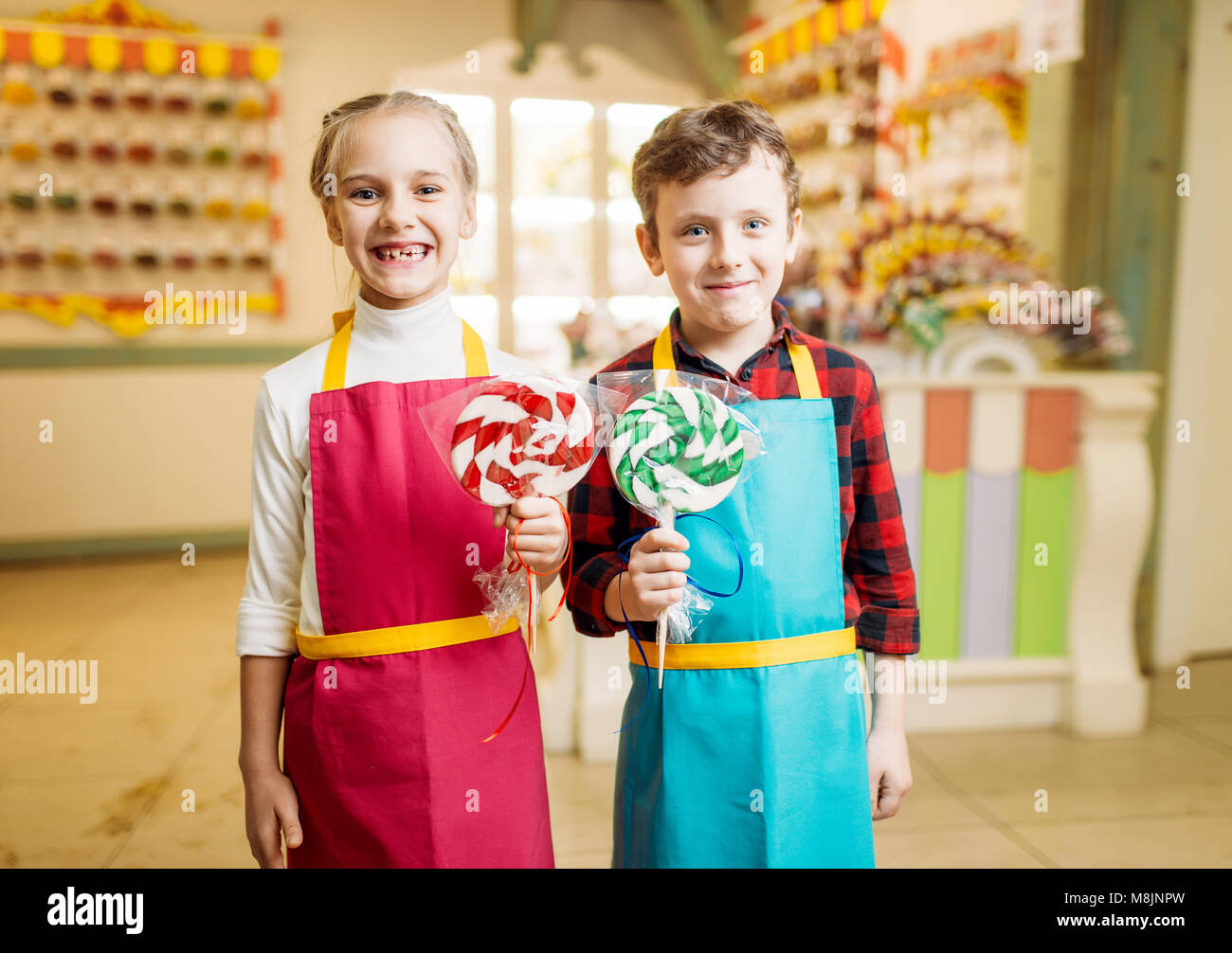 Little girl and boy holds in hands fresh lollipop. Children in workshop ...