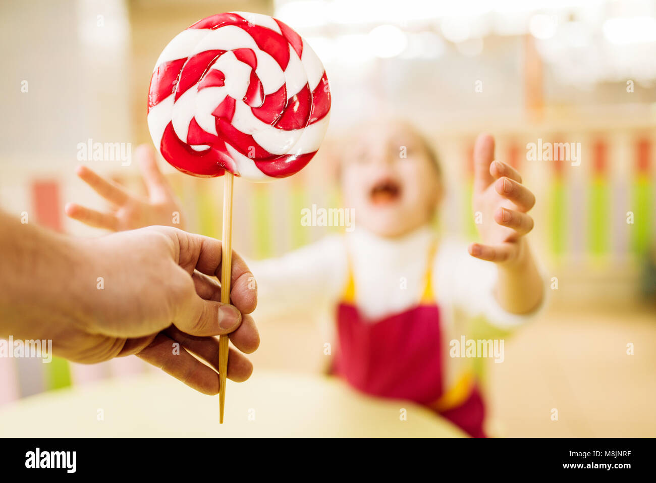 Hand gives handmade lollipop to happy little girl. Children in workshop ...