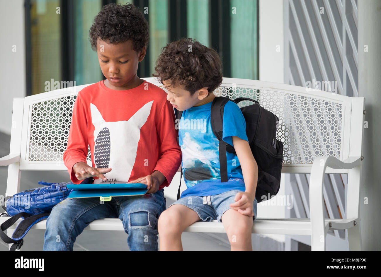 Two boy kid sitting on bench and playing game on tablet at preschoo ...