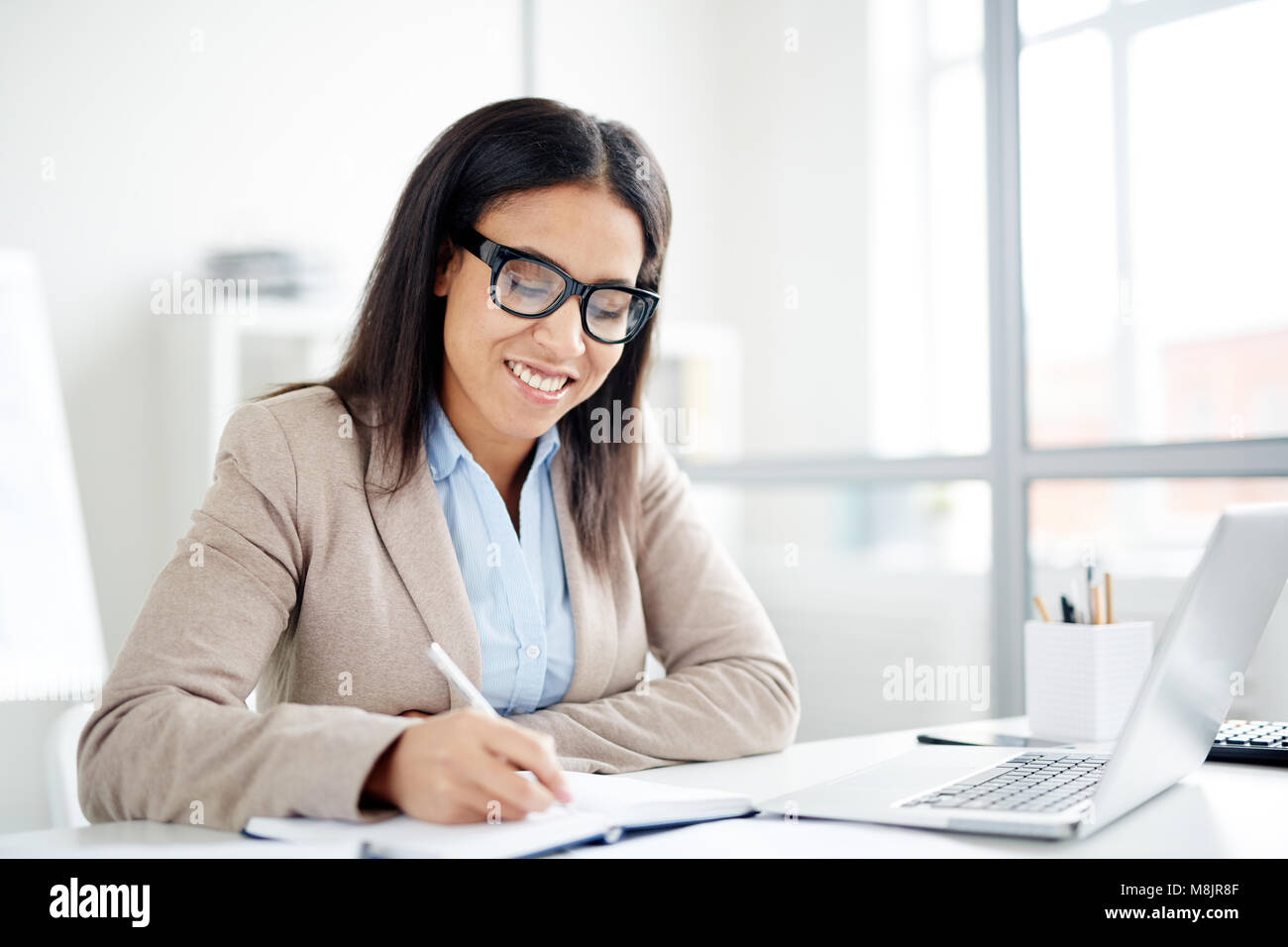 Smiling manager making notes at the office table Stock Photo - Alamy