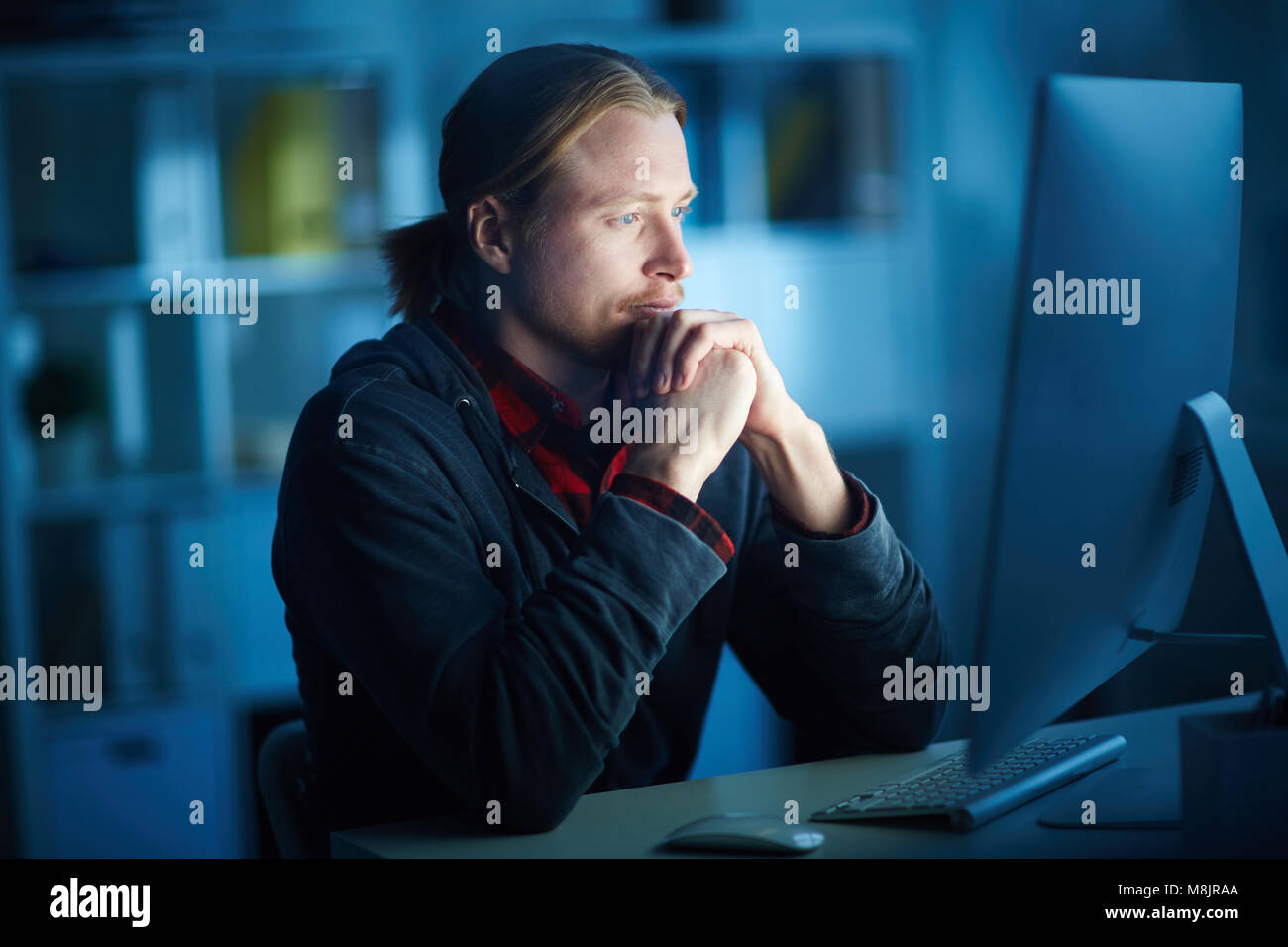 Serious man looking at a computer screen, in a dark office Stock Photo ...