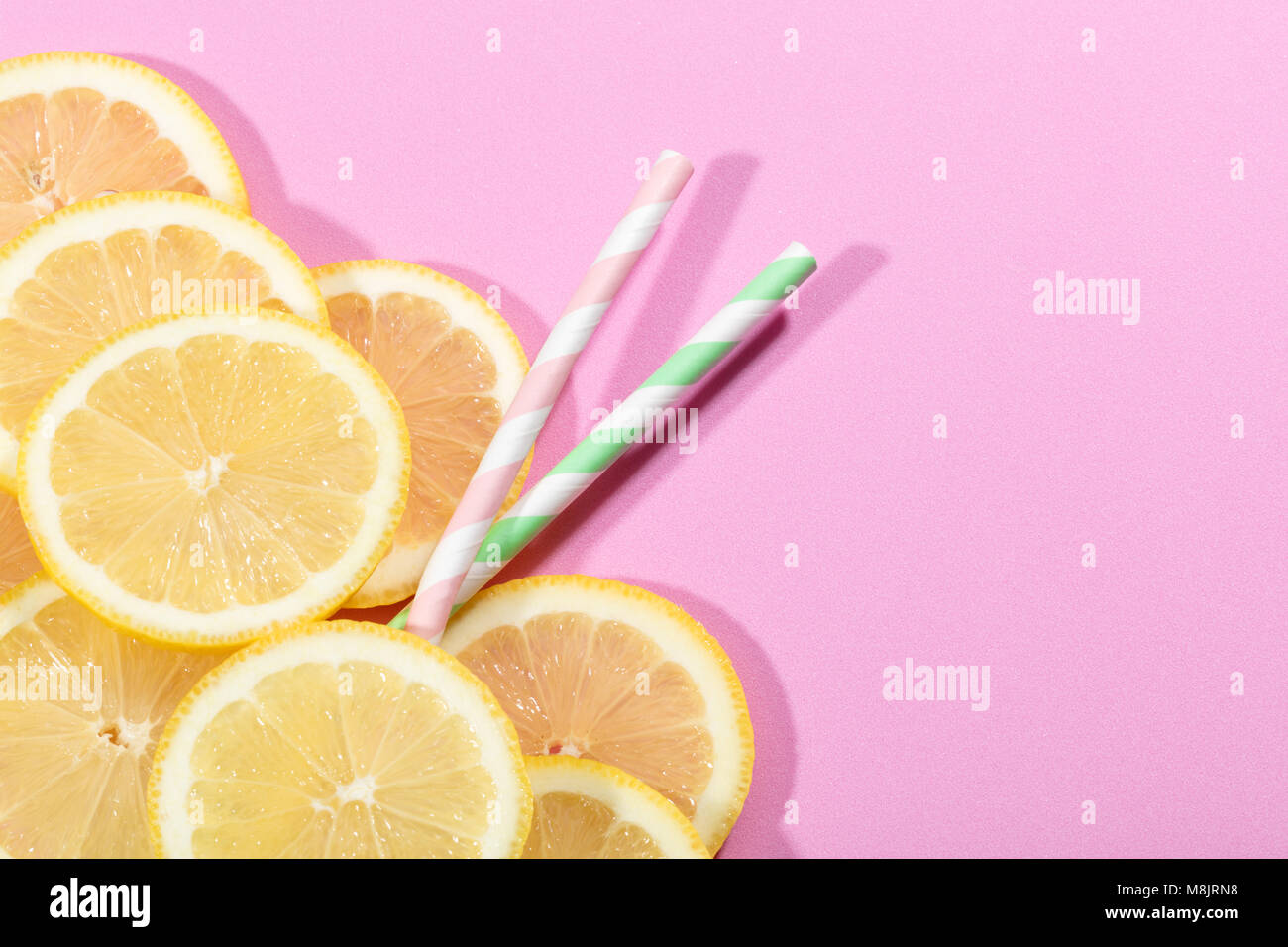 slices of lemon on pink colored background, with two stripped straws ...