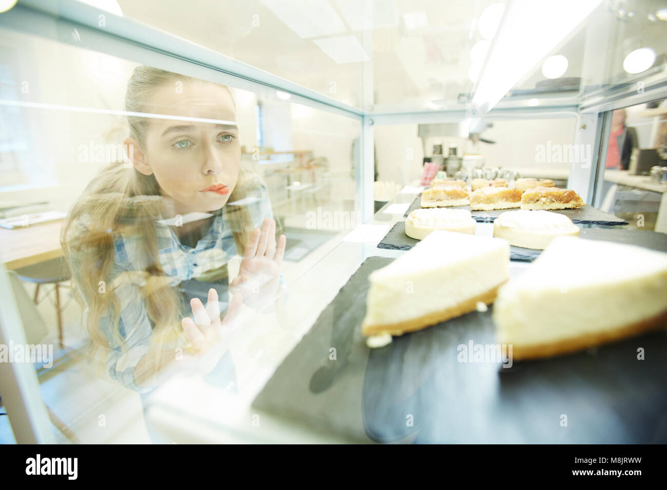 Young woman looking at sweet cakes with upset face Stock Photo - Alamy