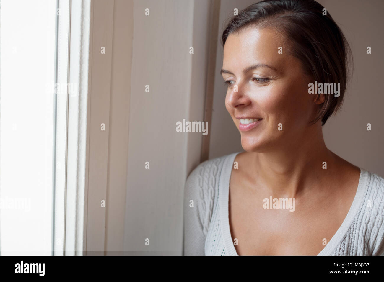 Portrait happy young woman looking out window hi-res stock photography ...
