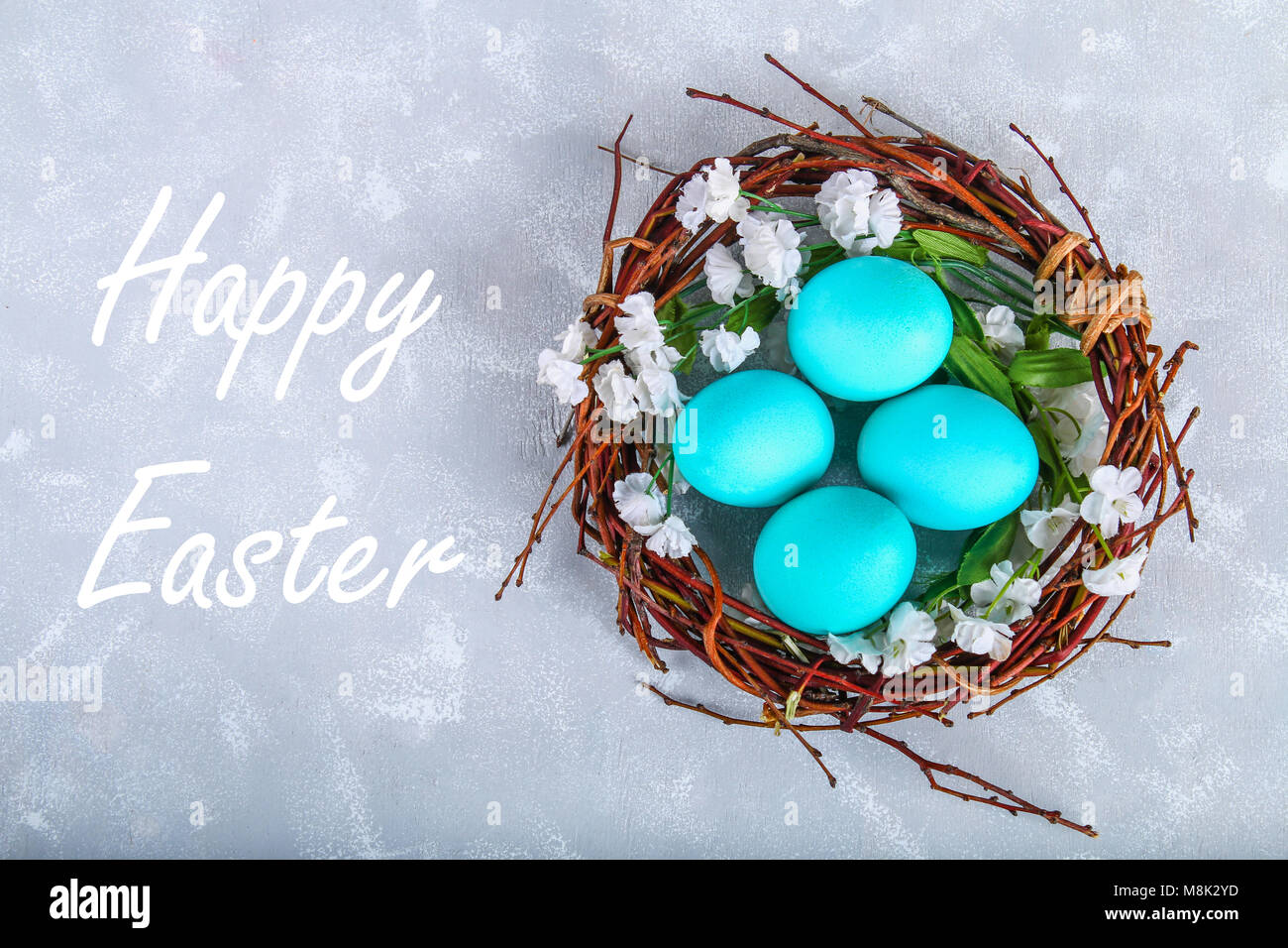 Blue easter eggs in a nest with white flowers on a gray concrete ...