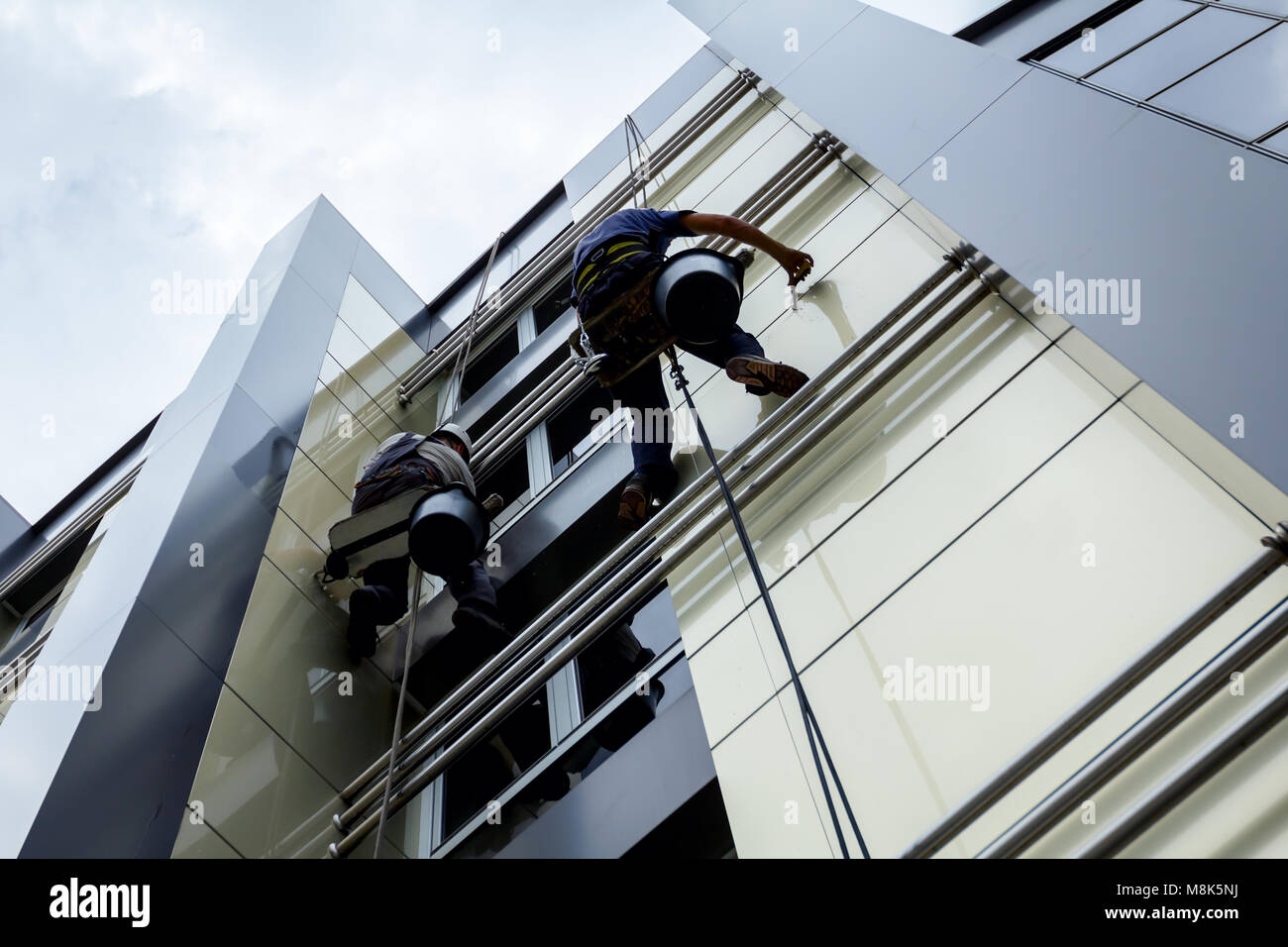Two industrial climbers are washing, cleaning facade of a modern office ...
