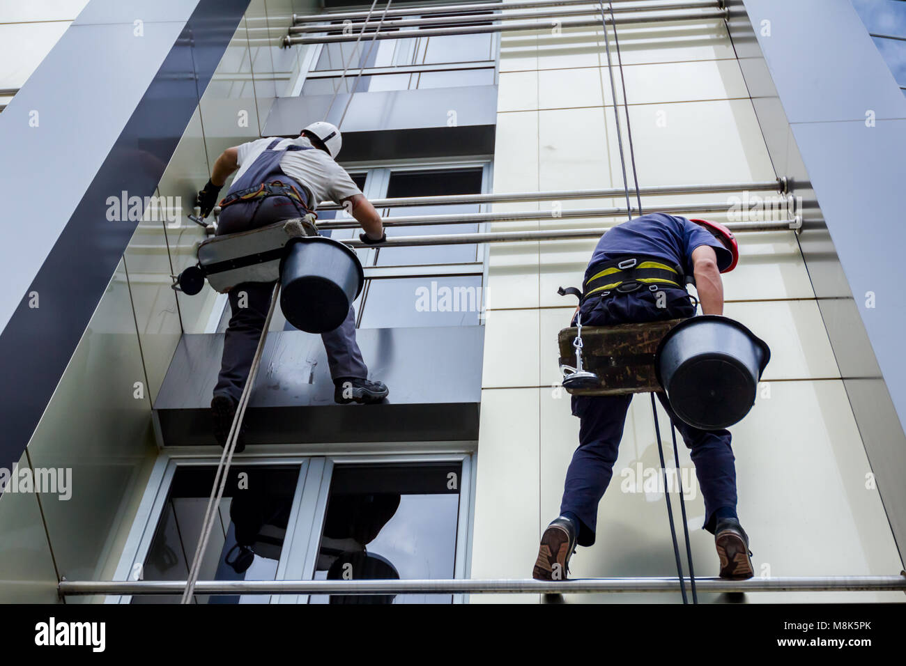 Two industrial climbers are washing, cleaning facade of a modern office ...