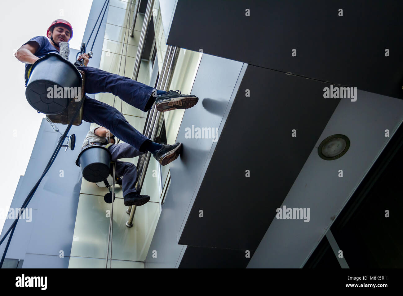 Two industrial climbers are washing, cleaning facade of a modern office ...