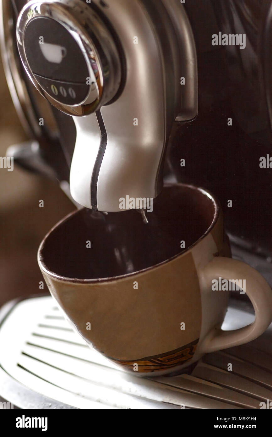 White cup standing on the grating of coffee machine with coffee pouring ...