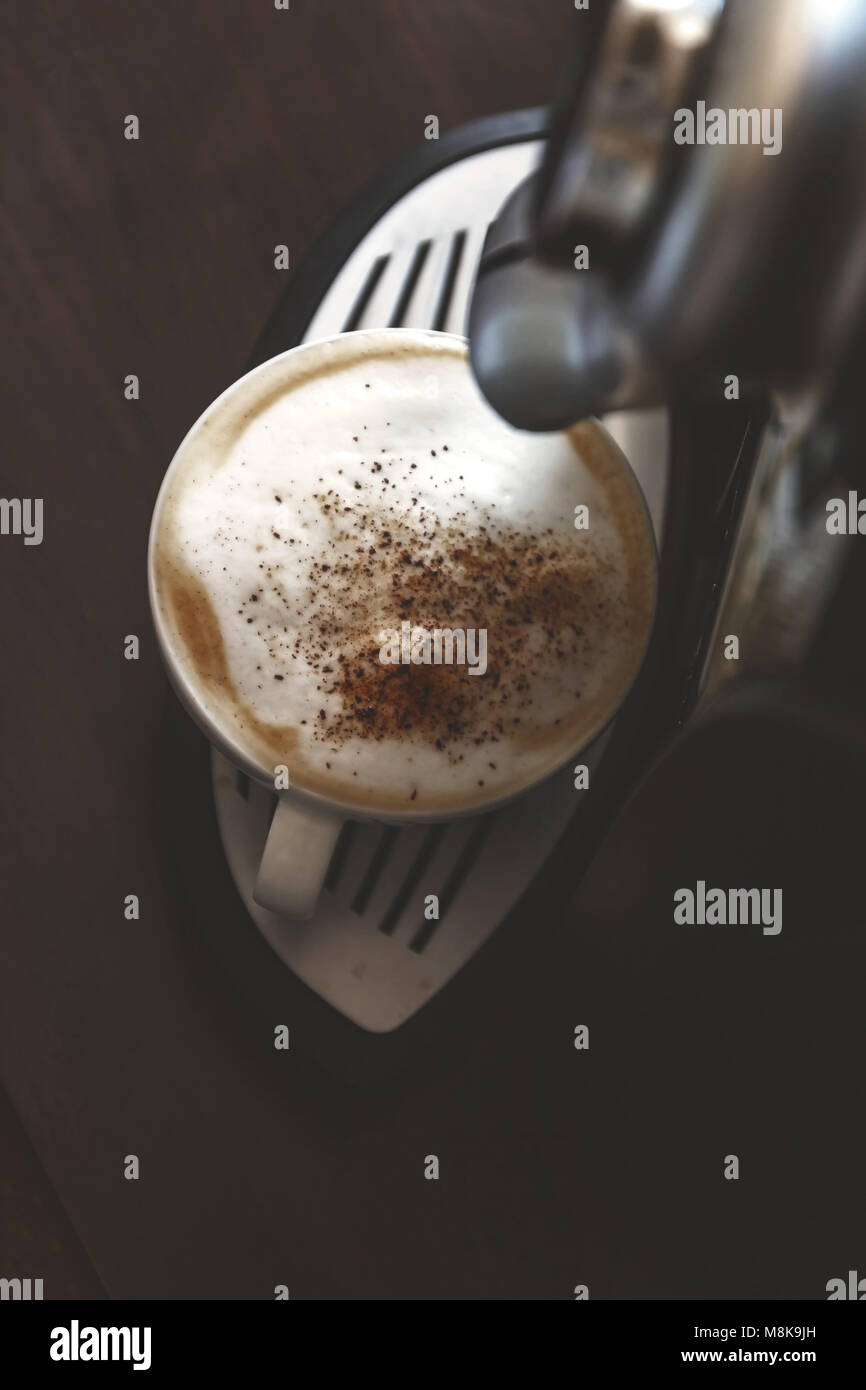 White cup standing on the grating of coffee machine with coffee pouring ...