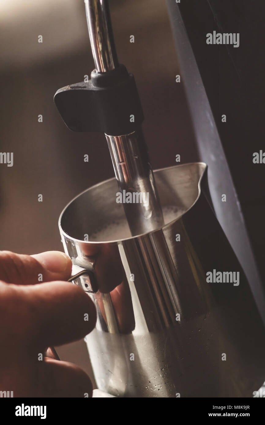 Professional bartender warming milk for cappuccino. Barista using coffee machine for latte art ...