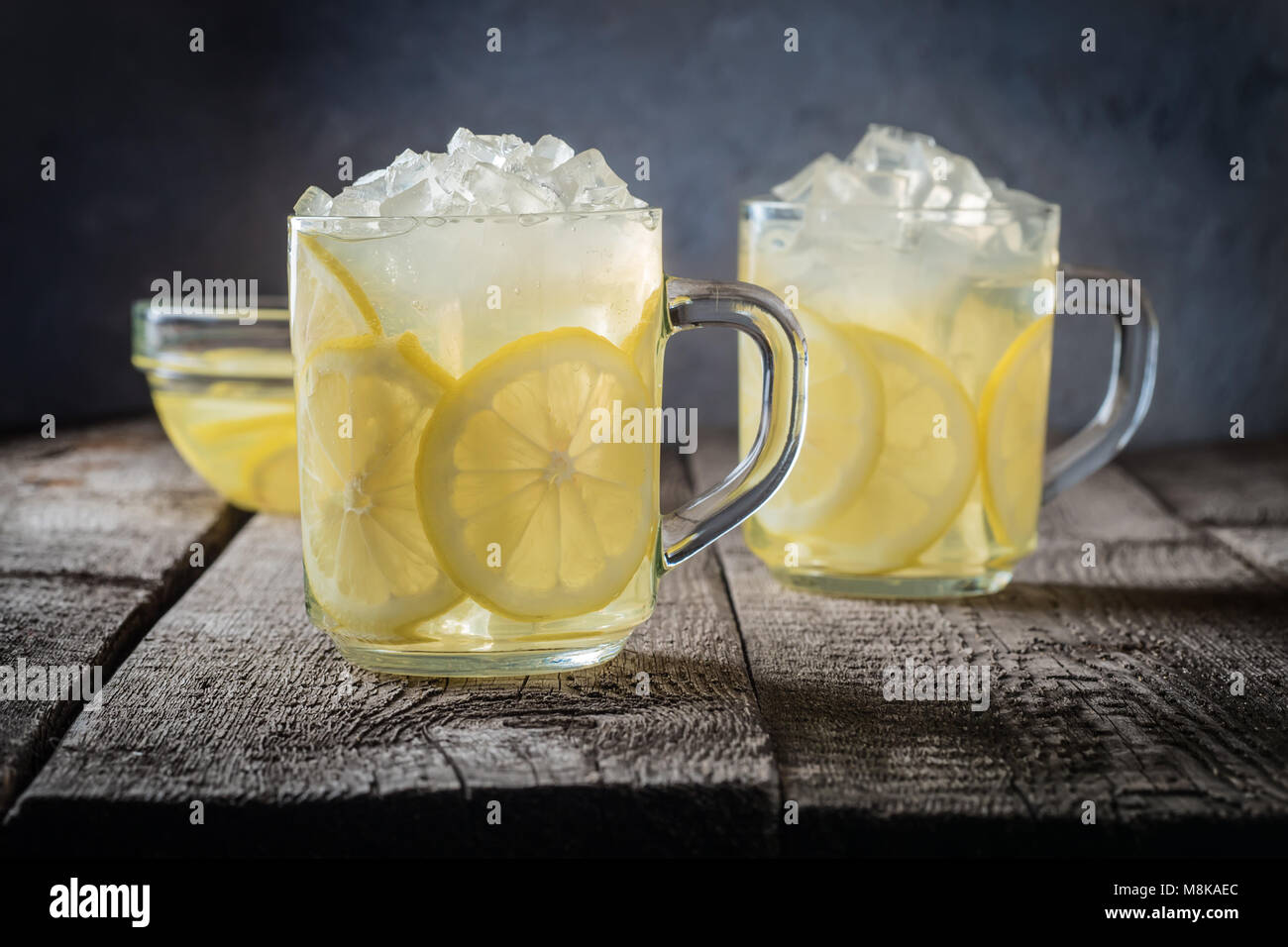 Two cups of lemonade and ice cubes crumbs on a wooden table background ...