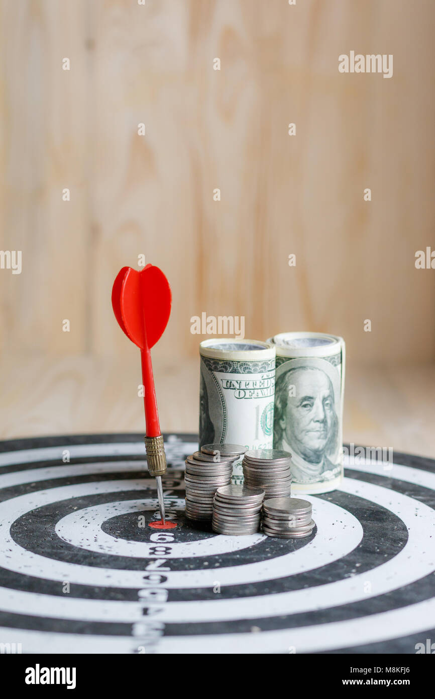 Red dart arrow hit the center target of dartboard and money coin ...