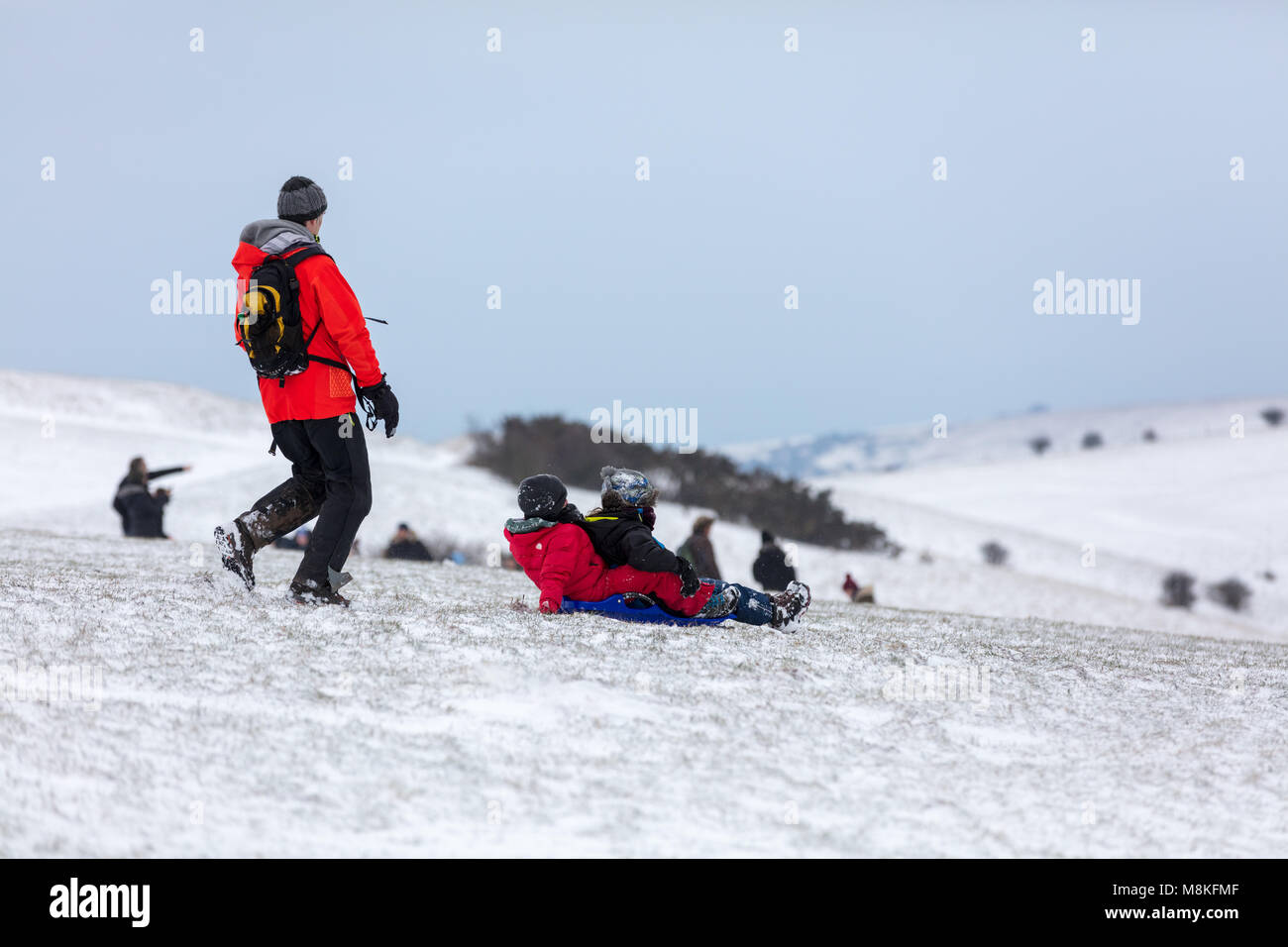 Two Boys on a sled with Adult Male in Red Jacket Standing Behind Them ...