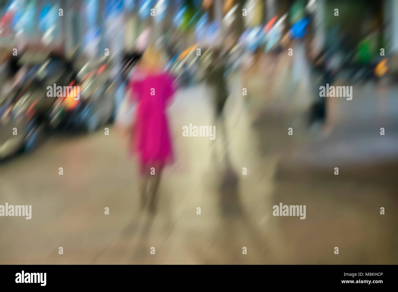 Abstract blurred silhouette of blond girl, back view in bright raincoat ...