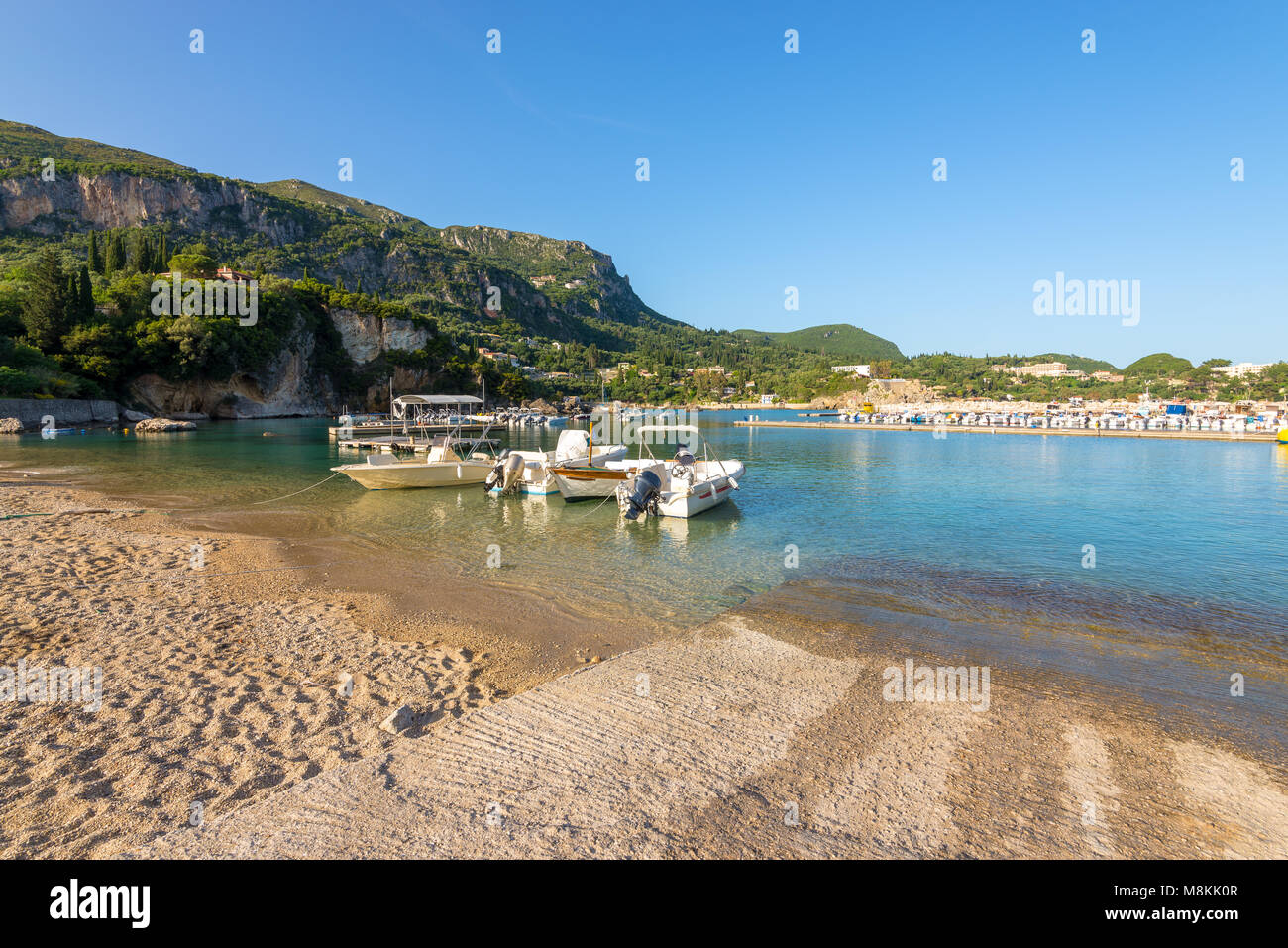 Boats moored at Alipa beach in Paleokastritsa bay with sand and crystal ...