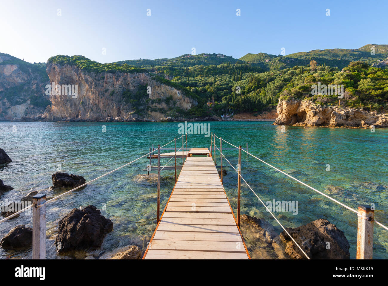 Wooden pier in Paleokastritsa bay with sand and crystal sea water ...