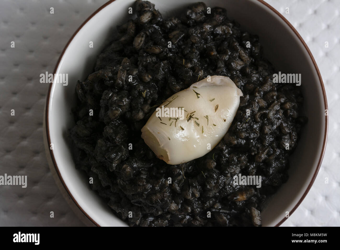 Black rice with cuttlefish, on black cement dish and grunge background ...
