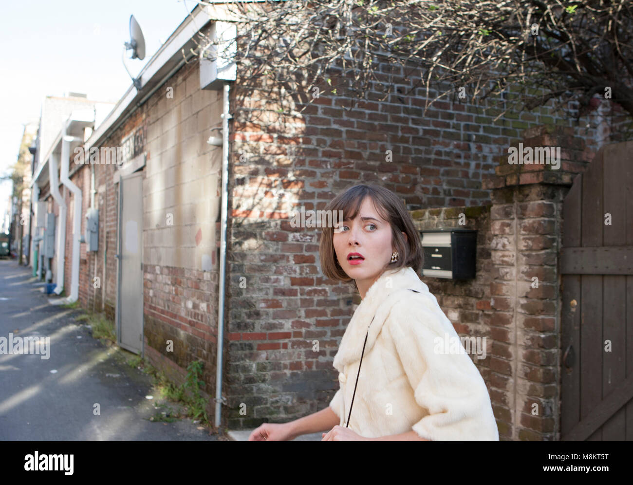 A well dressed woman, standing alone outside, looking back in fear ...