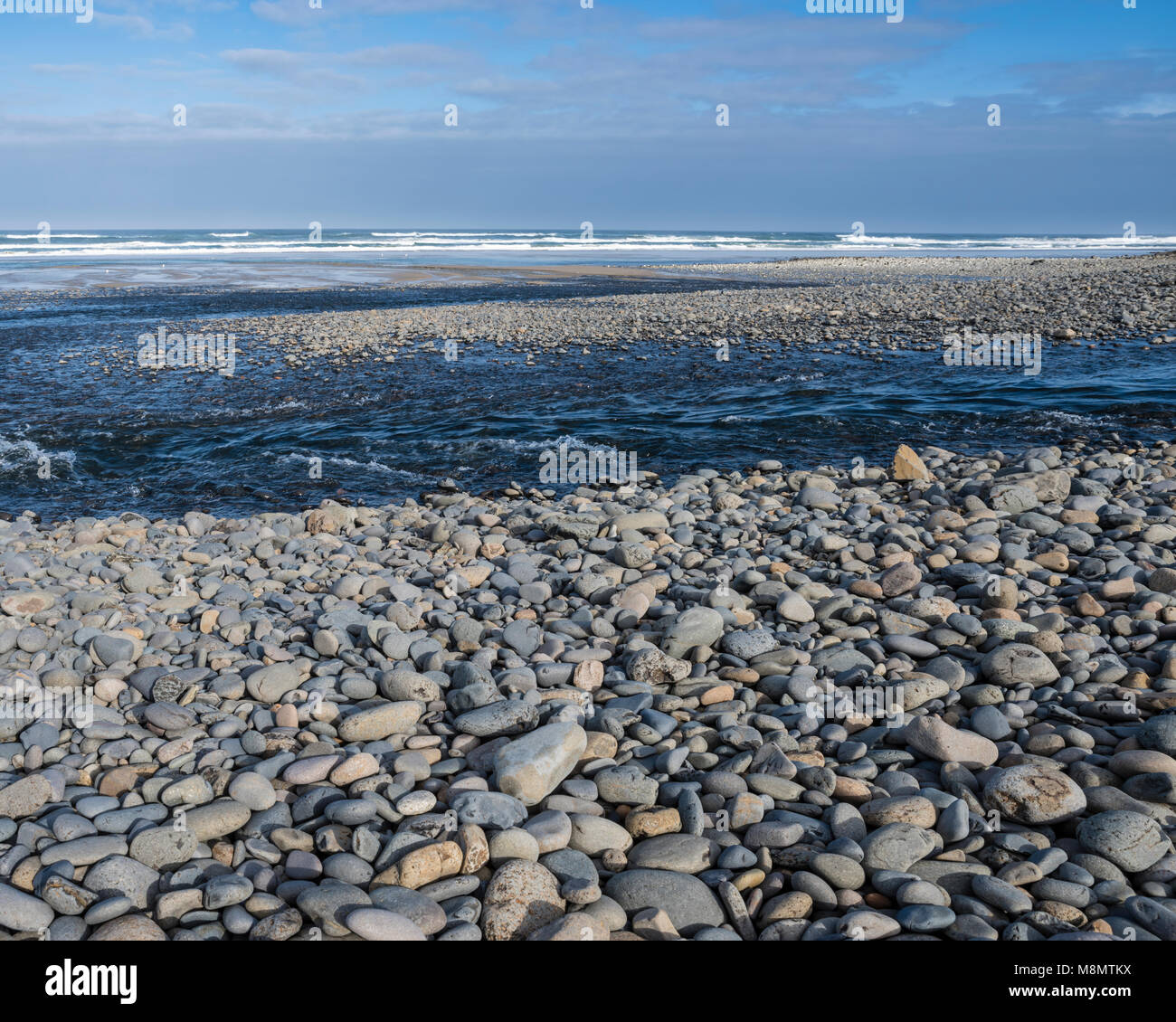 Pebble strewn beach with a fresh water stream entering the ocean ...