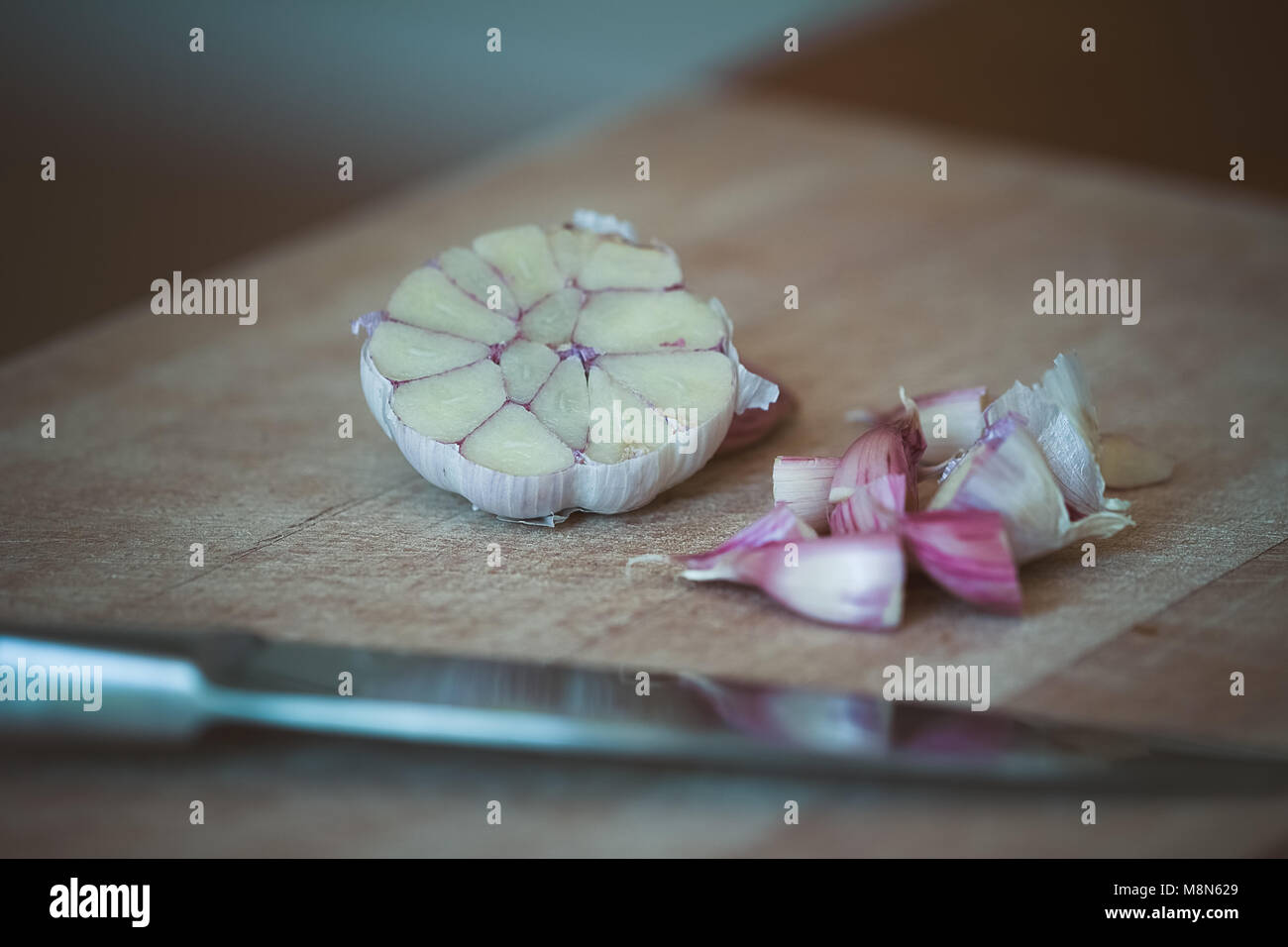 Raw garlic (Allium sativum) being chopped on a wooden chopping board ...