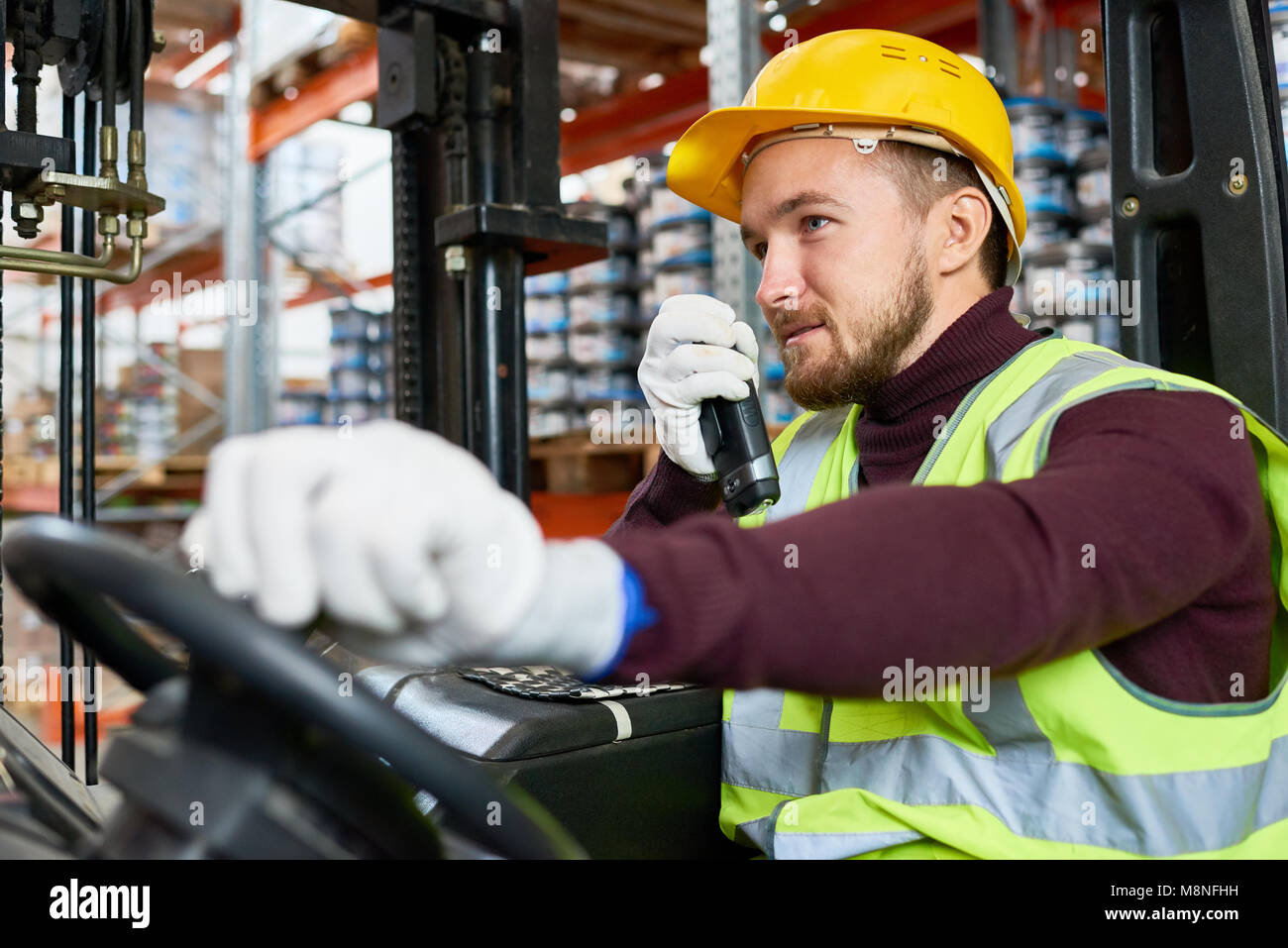 Waist up portrait of young man sitting in forklift and using walkie ...