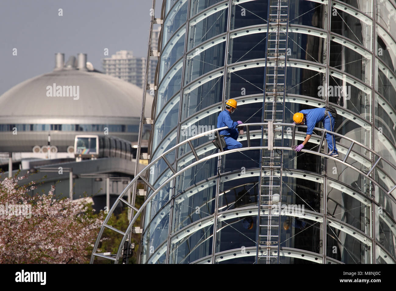 2 Japanese workers wearing blue overalls and yellow helmets performing ...