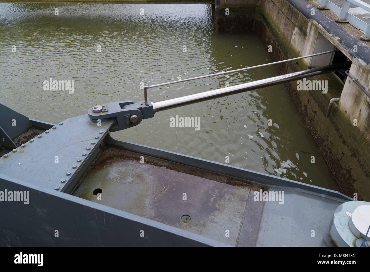 Heavy steel floodgate of a sluice being opened by a hydraulic cylinder ...