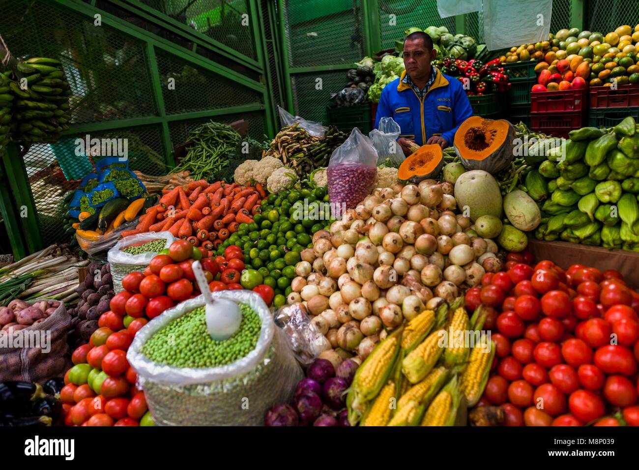 A Colombian vendor, holding a corn, stands behind the piles of ...