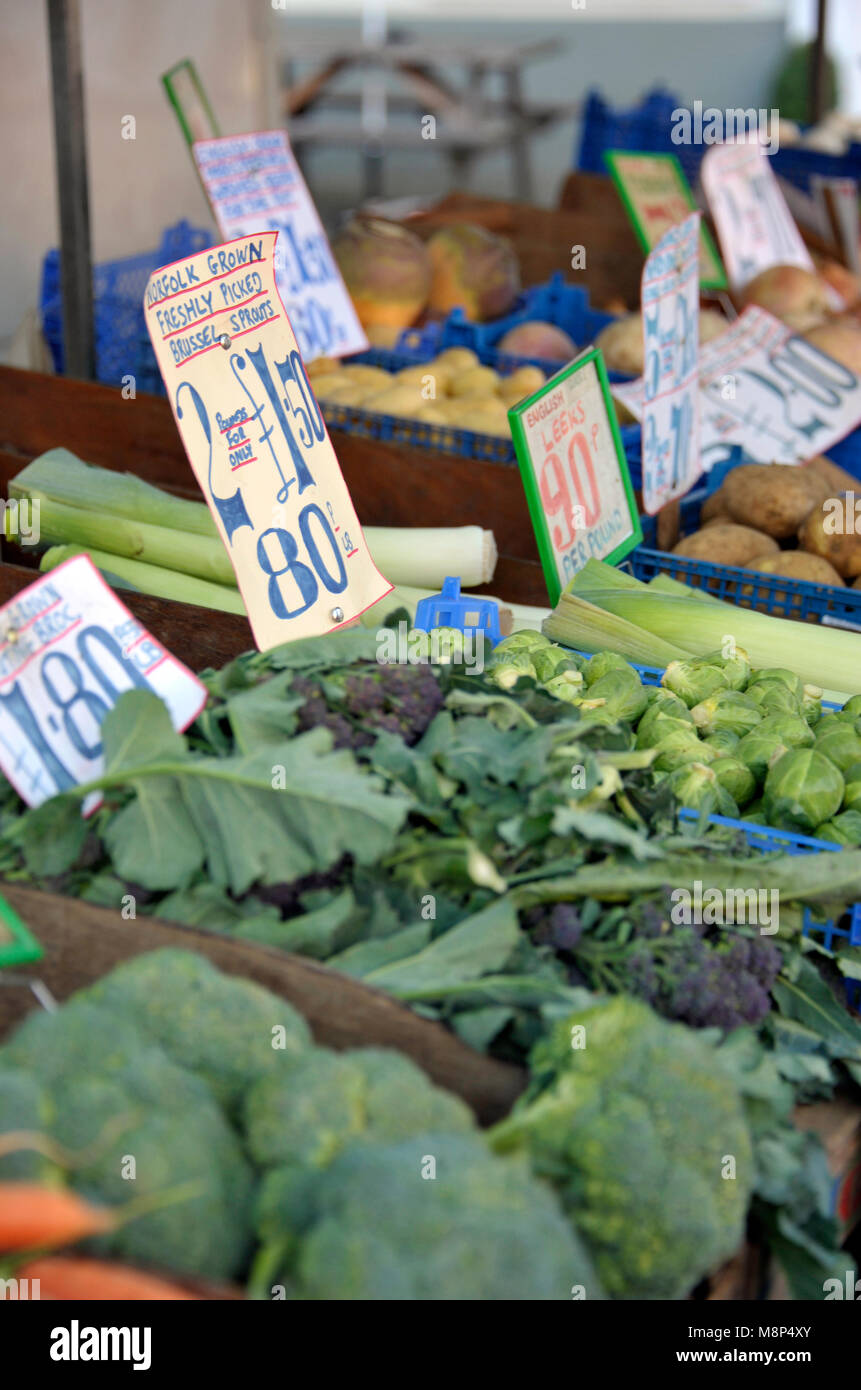 Greengrocer market trader vegetable stall with green brassicas, leeks ...
