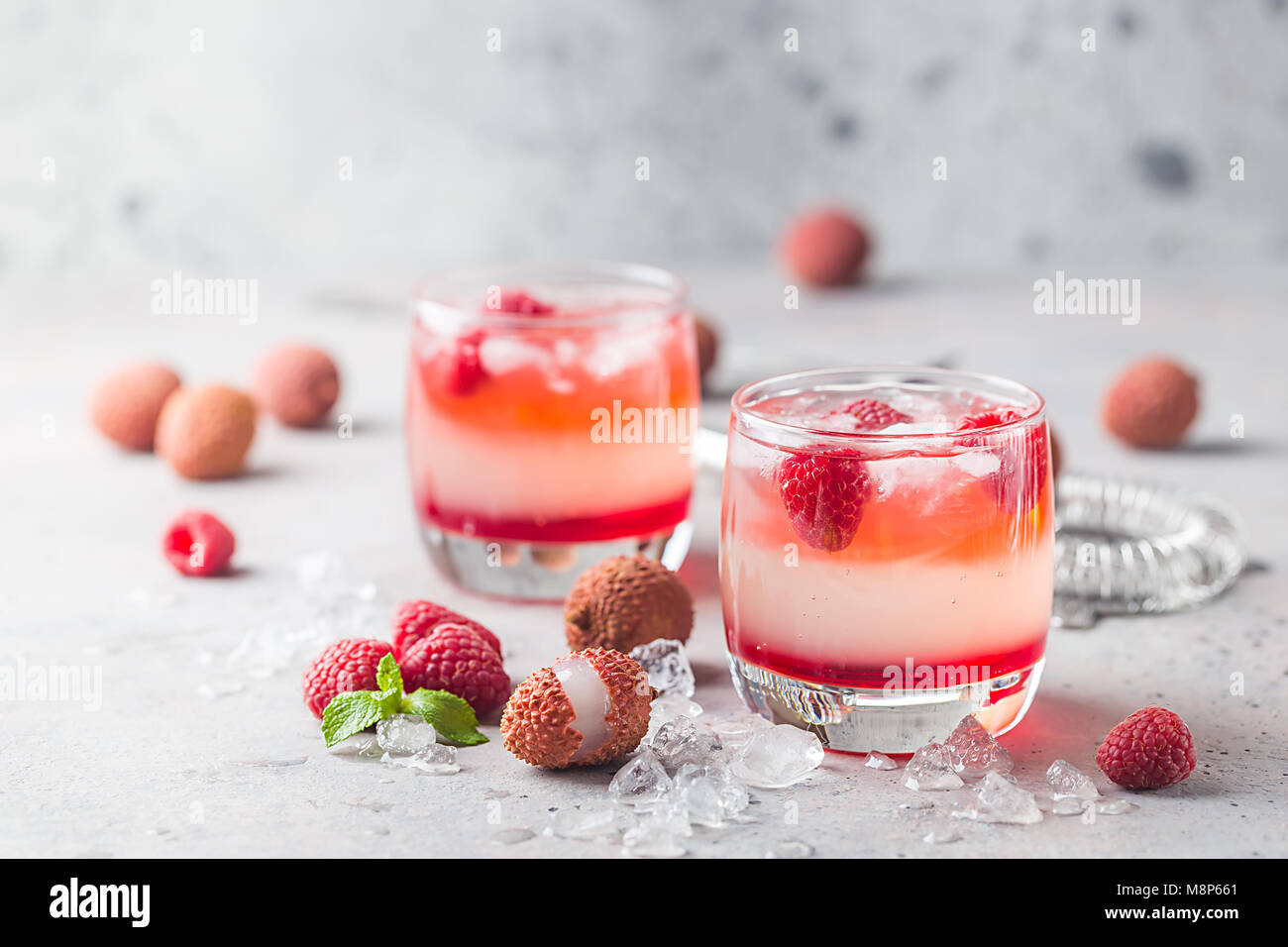 Refreshing cold lychee and raspberry cocktail in a glasses with ice and berries over gray ...