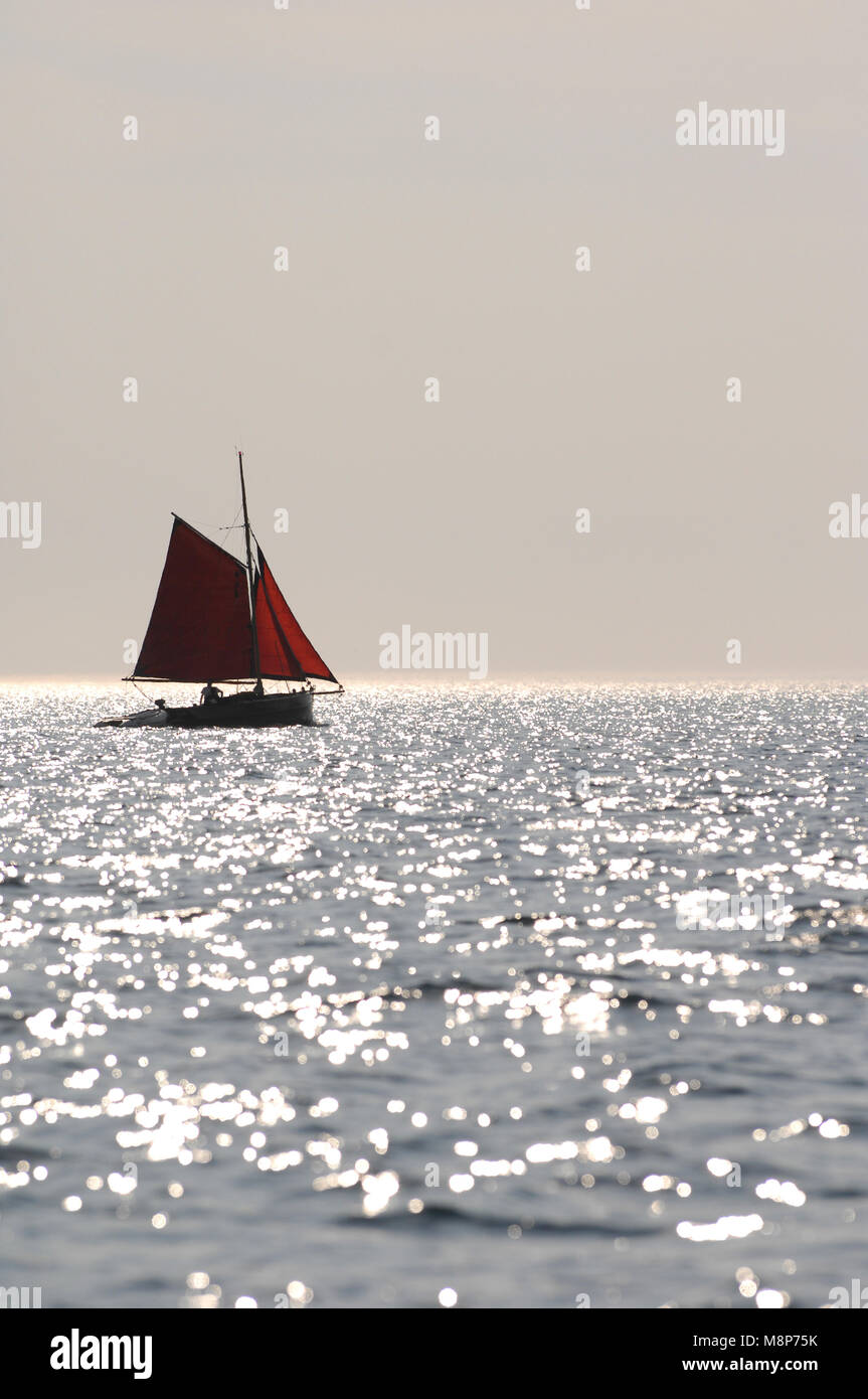 Beautiful red sailed boat on shimmering shiny water sailing left to ...