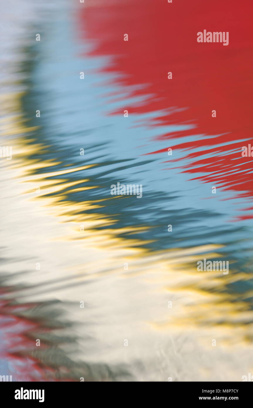 Red blue yellow & white reflections of the hull of a boat in clear blue ...
