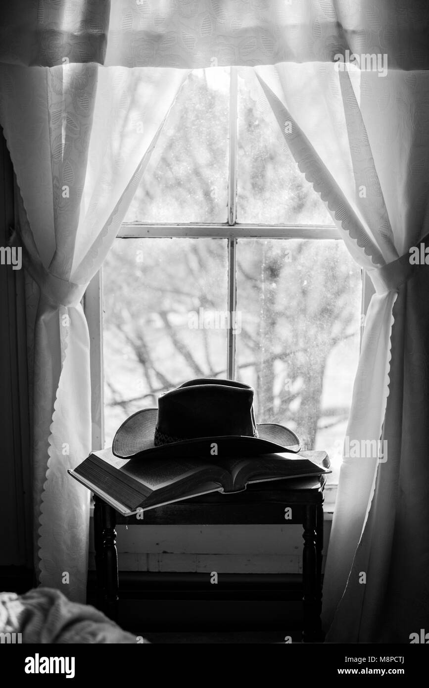 A cowboy hat and a Bible sits in a window sill with the sun shining ...