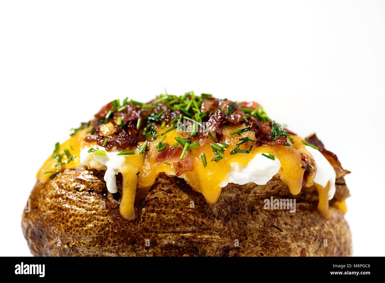 side view of a loaded baked potato with chives, bacon, cheddar cheese ...