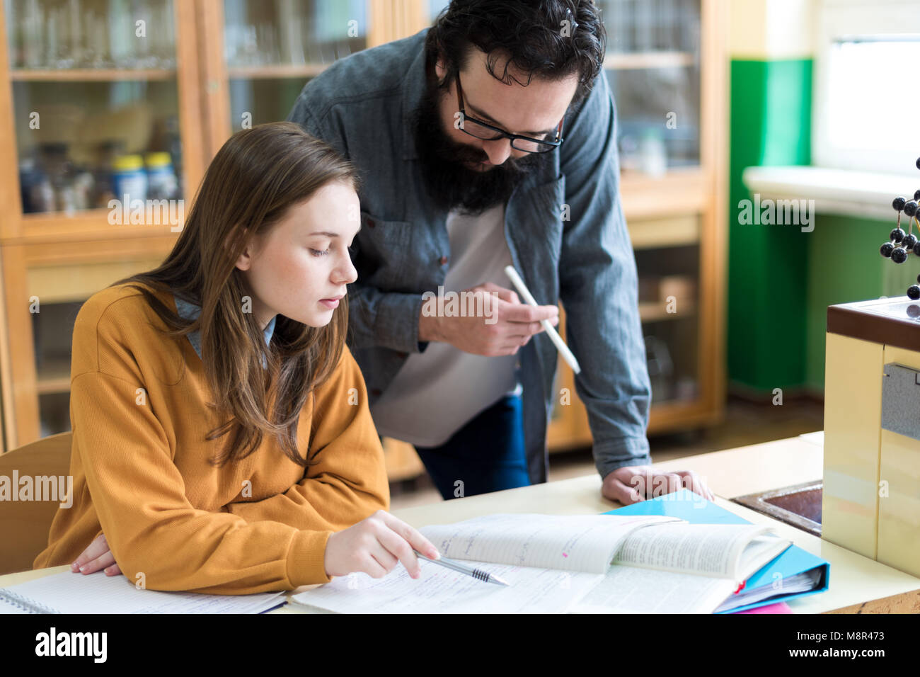 Young teacher helping his student in chemistry class. Education ...