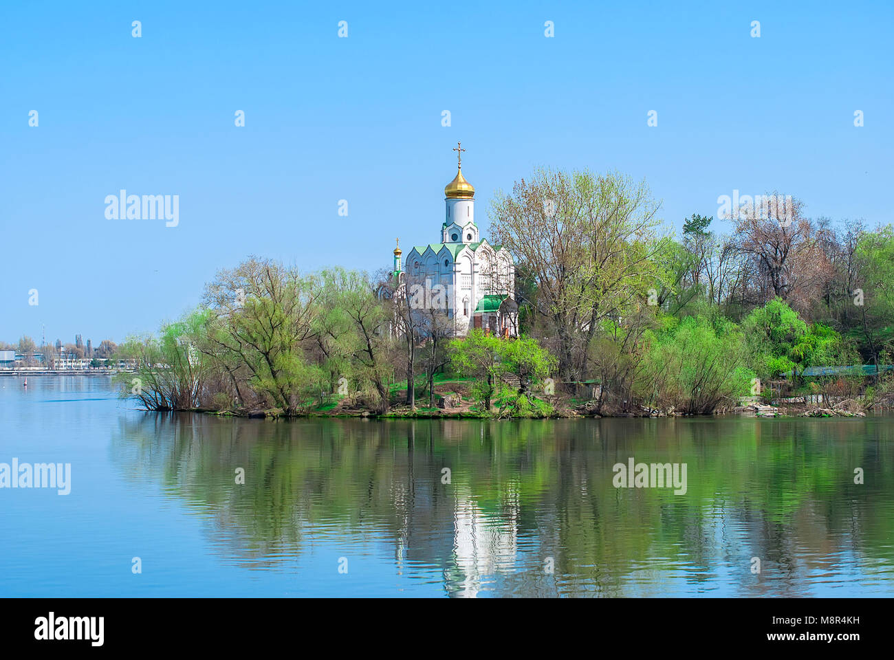 Church in the spring trees on the bank of the river, blue sky and ...