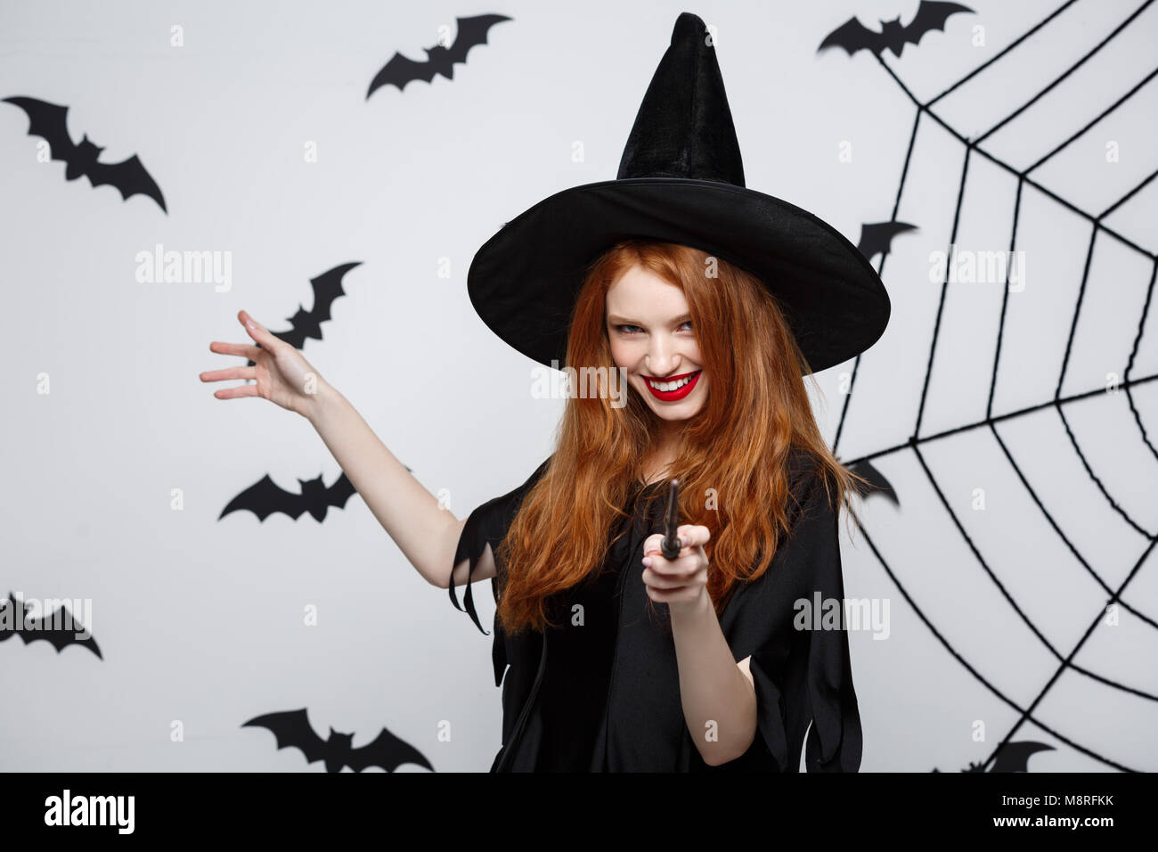 Halloween Concept - Beautiful Witch playing with magic stick on grey ...