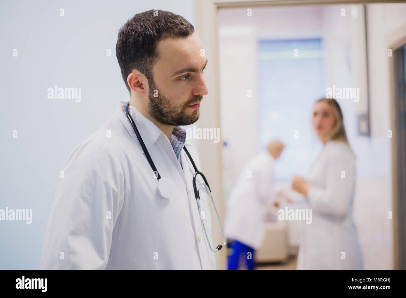 Side view of thoughtful young doctor in medical uniform listening to ...