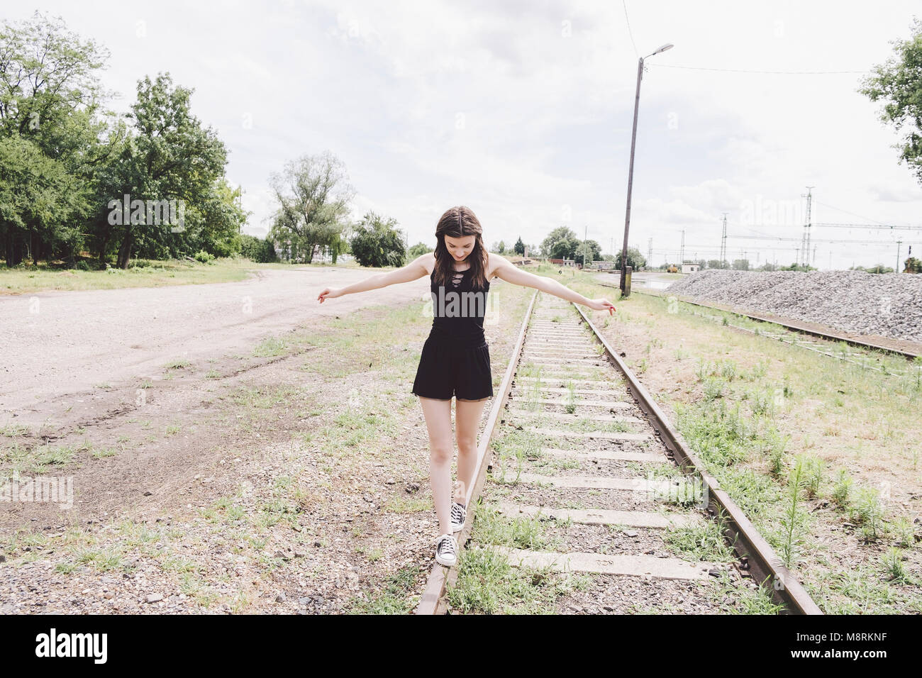 Full length of young woman with arms outstretched walking on railroad ...