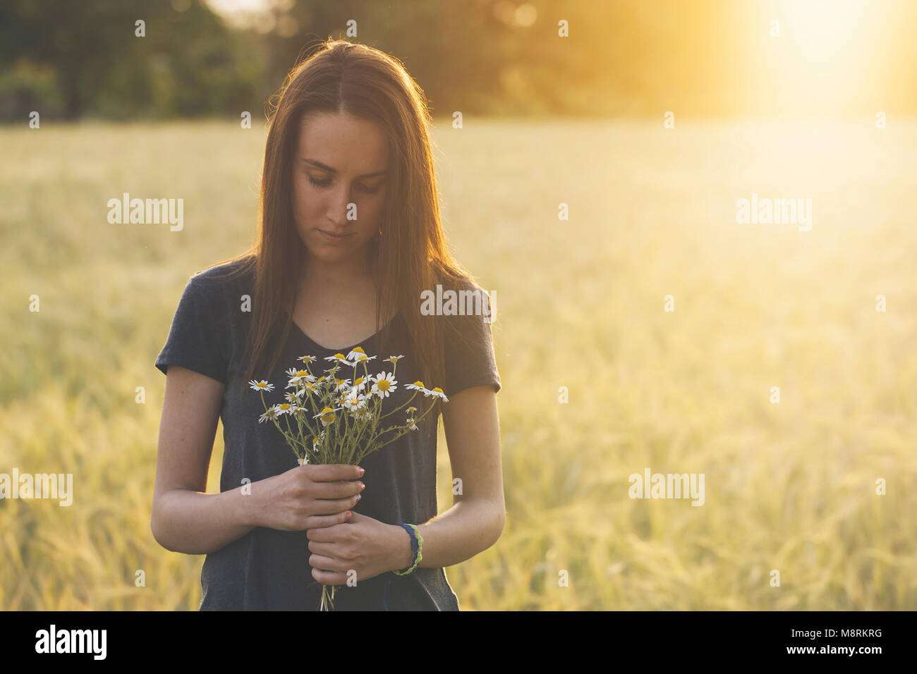 Young woman holding daisy flowers while standing on field during sunny ...