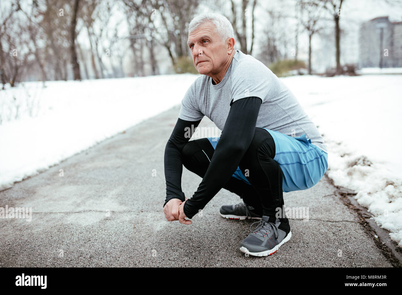 Active senior making pause crouching, during stretching and doing ...