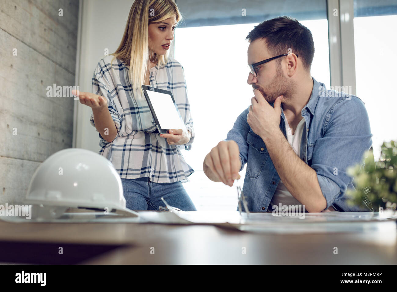 Young worried architect colleagues talking and analyzing blueprints ...