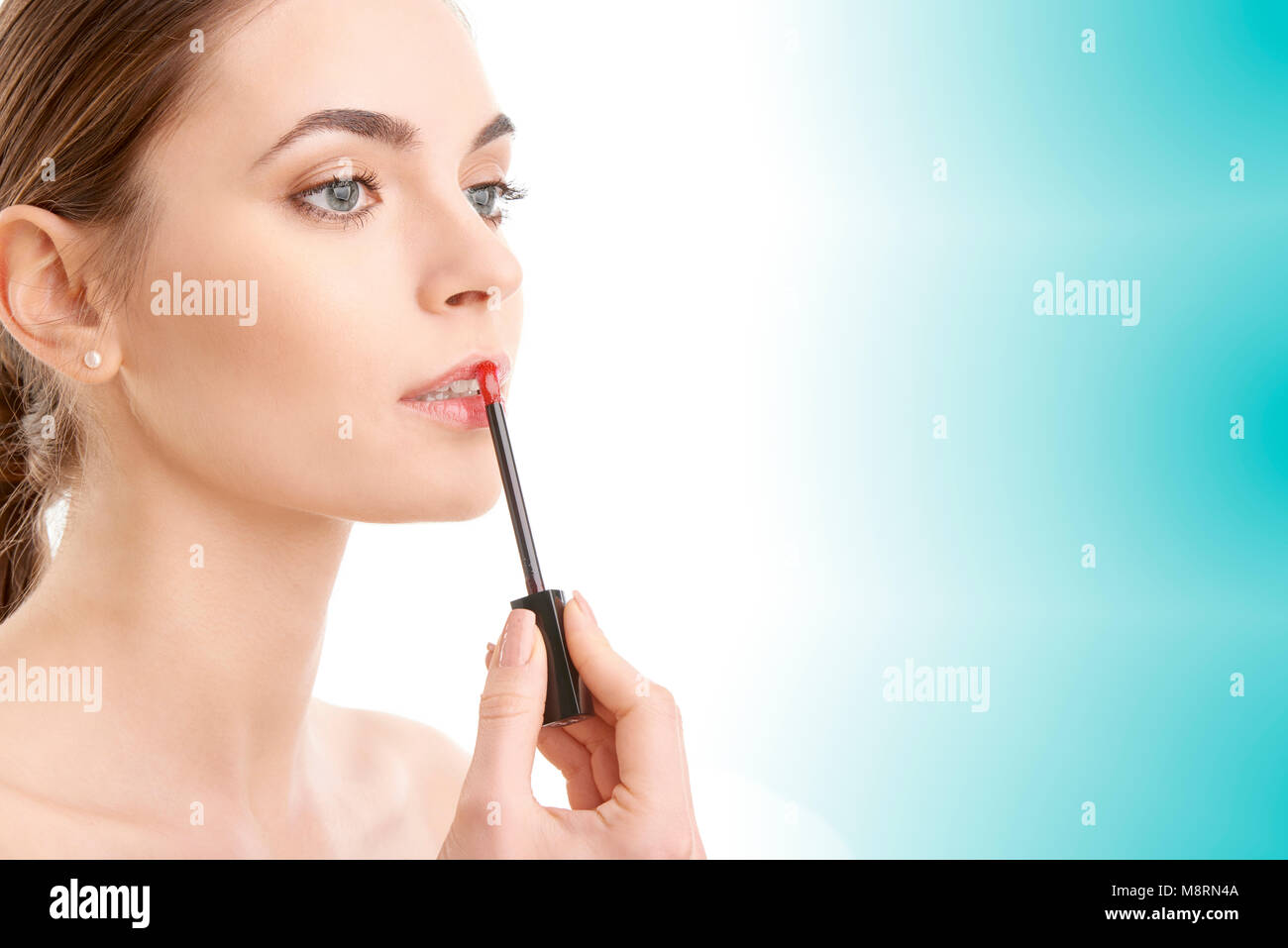 A young woman applying pink lipstick with an applicator while standing ...