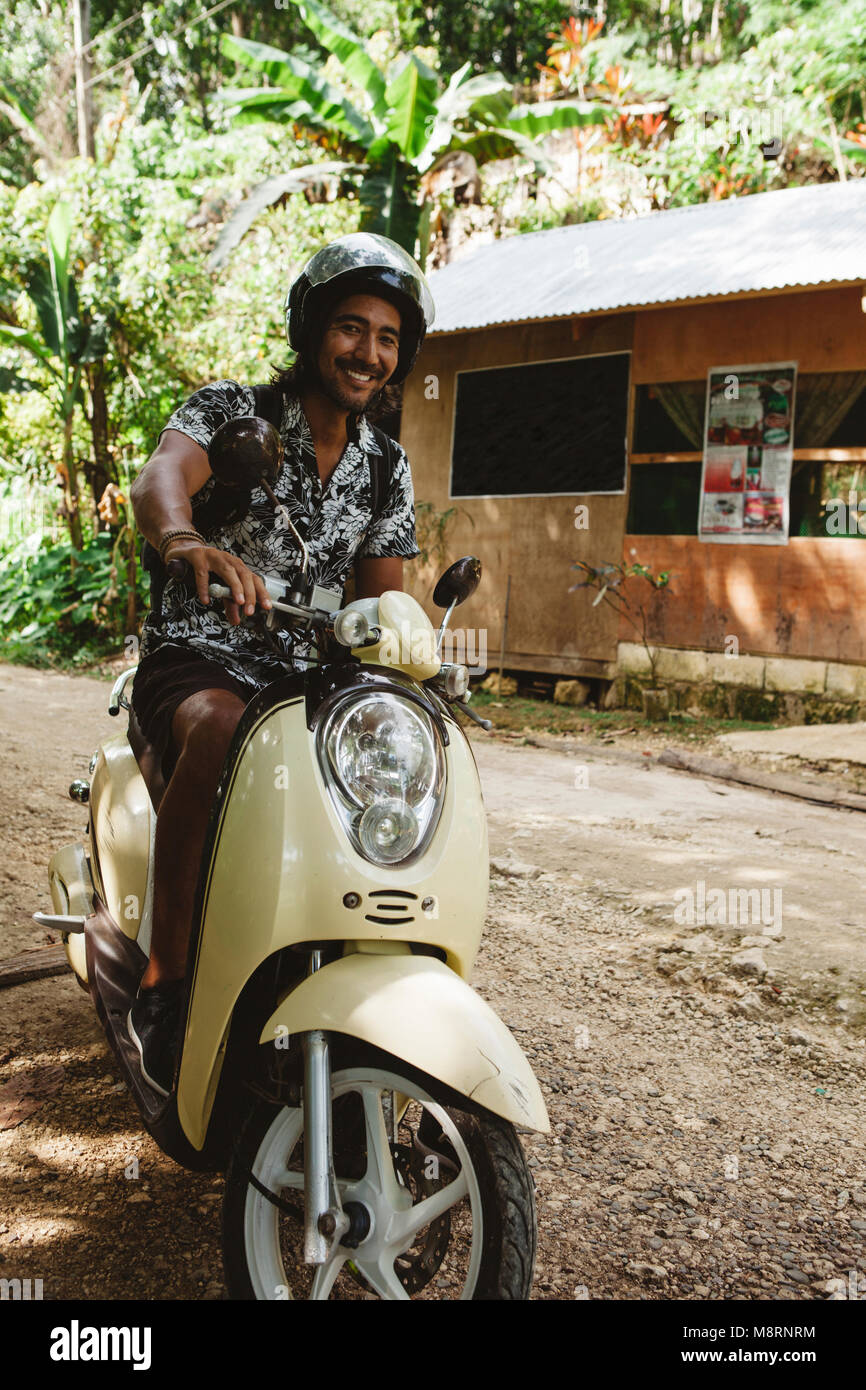 Portrait of cheerful man wearing helmet while driving motor scooter on ...