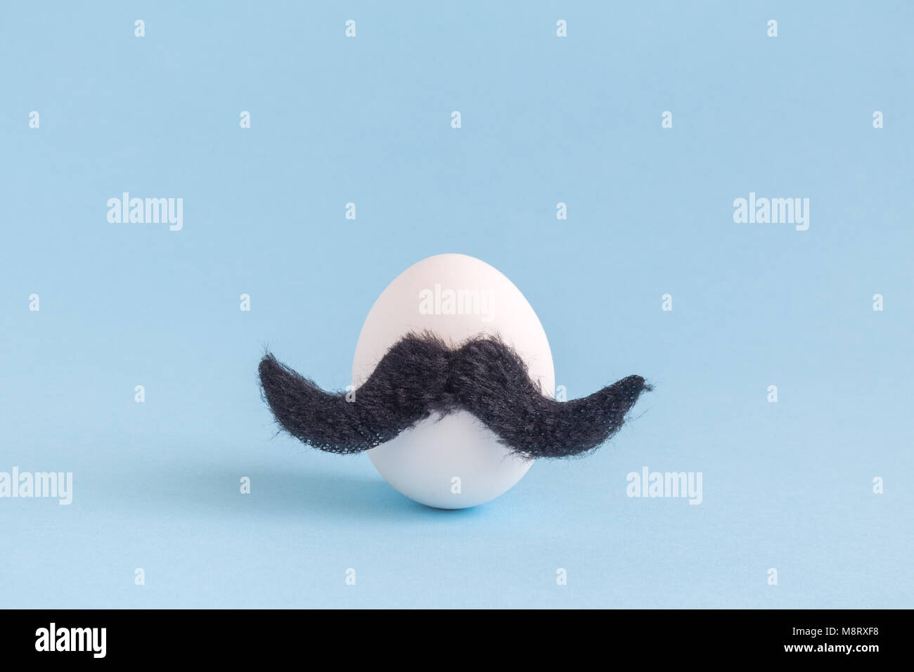 White egg with hipster mustache against pastel blue background. Minimal ...