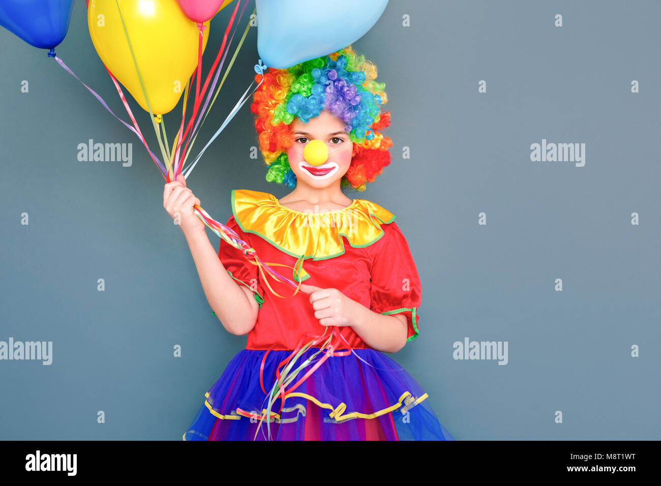 Girl clown holding lots of balloons getting ready for carnival. Studio ...