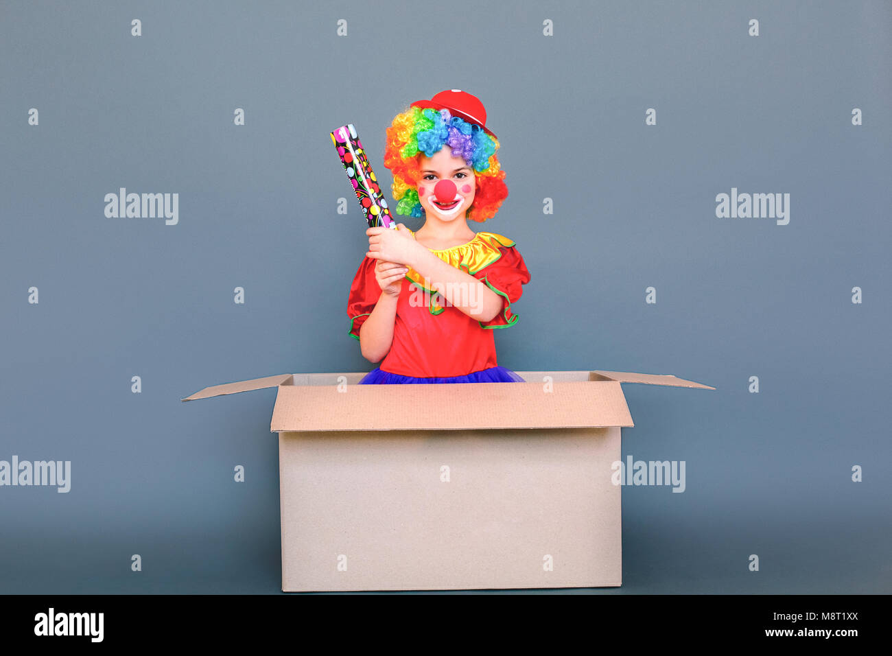 Funny kid clown playing in cardboard, shooting party popper confetti ...