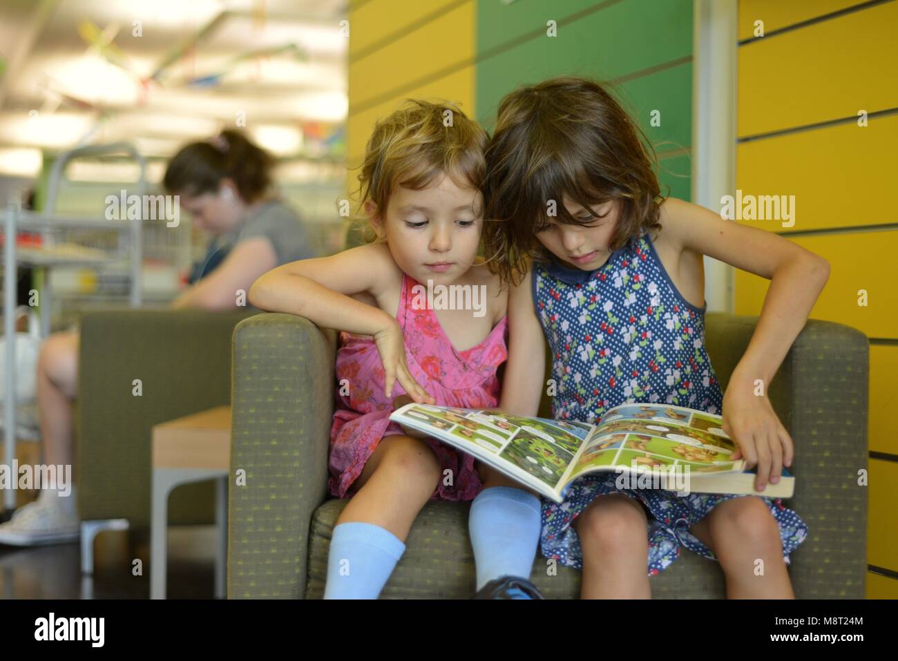 Two girls reading a book in a public library, CityLibraries Aitkenvale ...